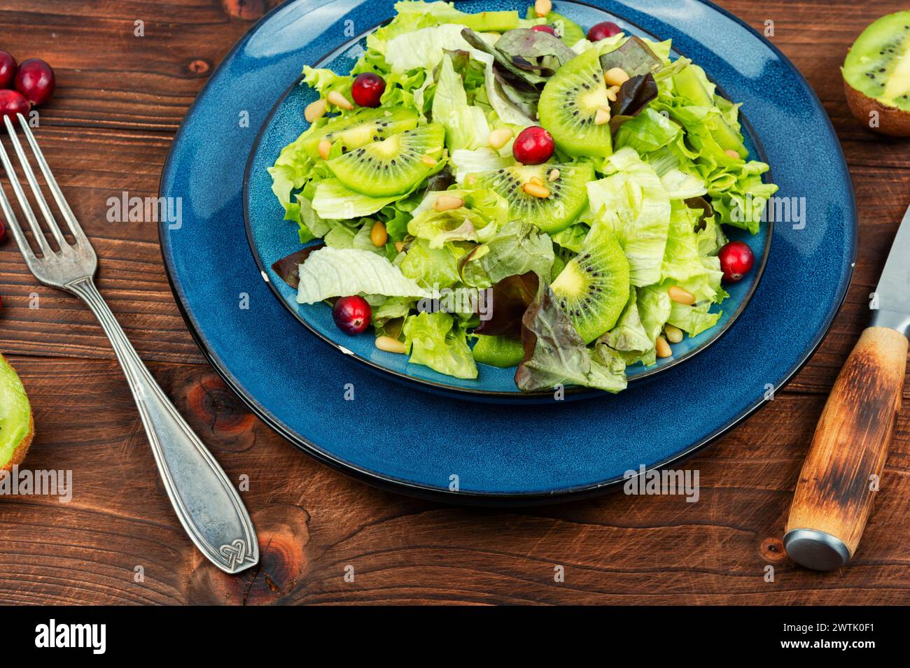 Vegan salad of kiwi, greens, berries and pine nuts on wooden table ...