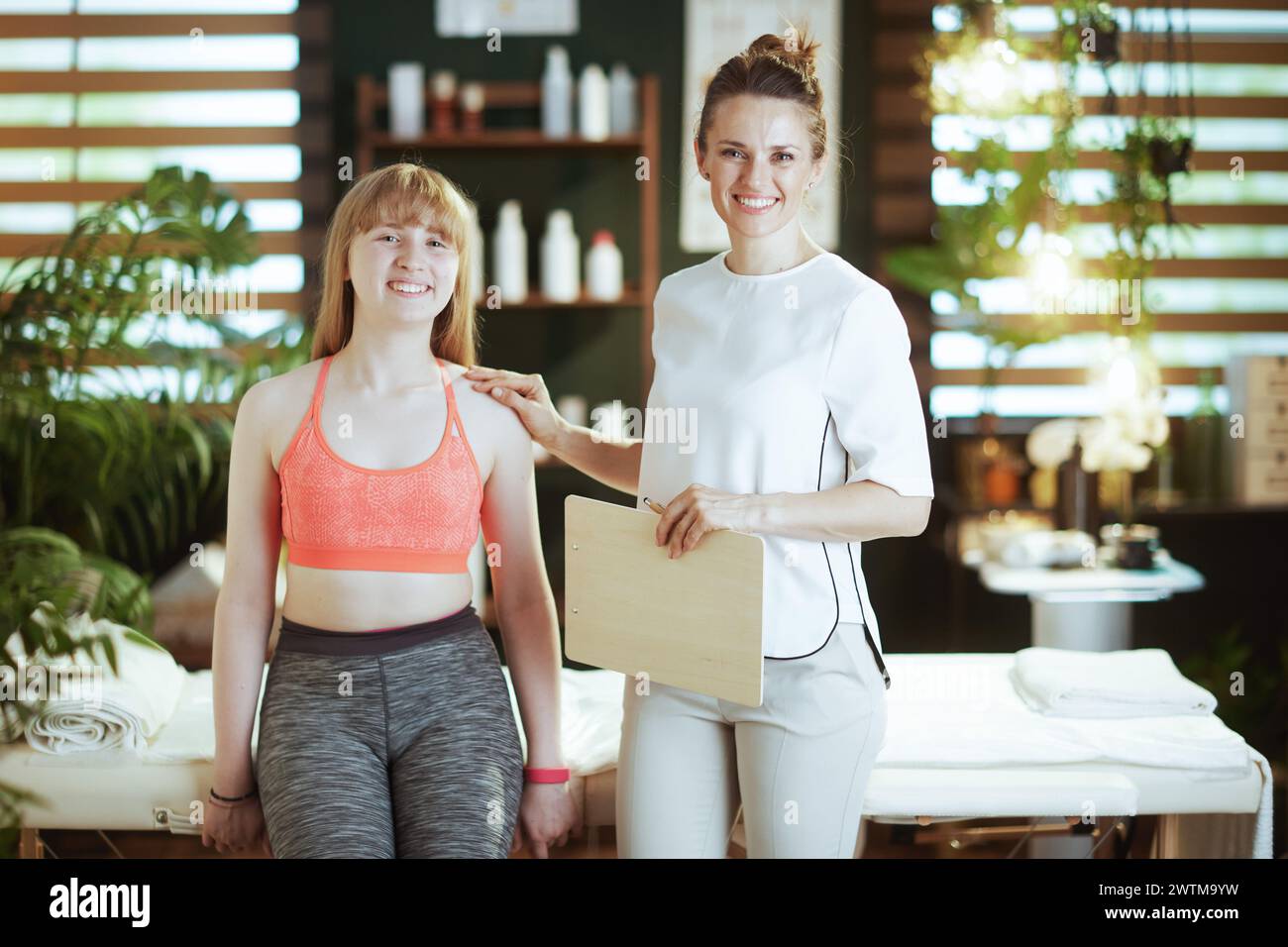 Healthcare time. smiling massage therapist woman in massage cabinet with clipboard and teenage ...