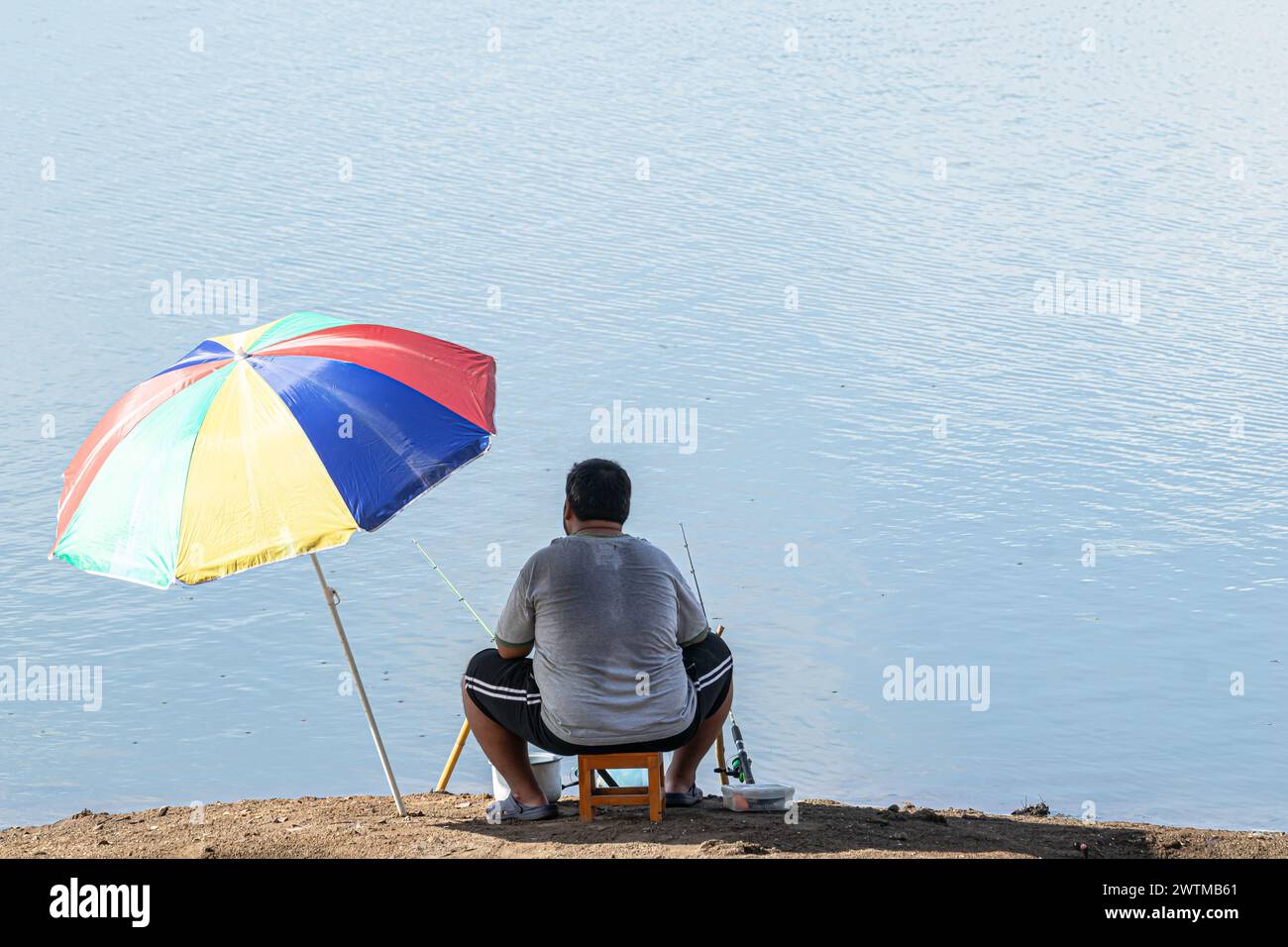 A man is sitting fishing on the bank of a river. man sitting under an ...