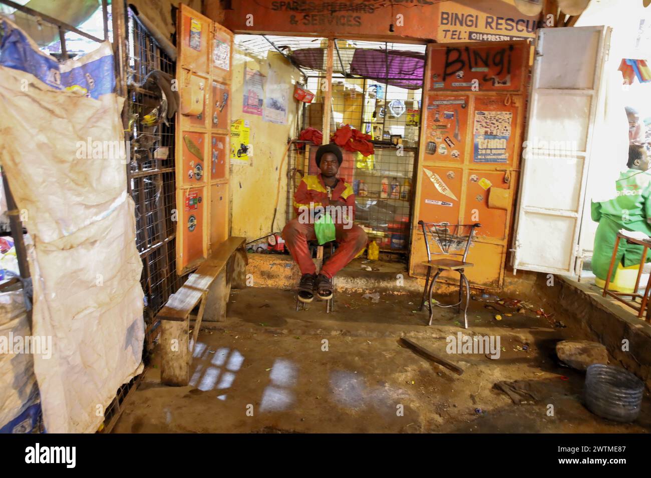 A motorcycle mechanic is seated waiting outside his shop in Kibera Slum ...