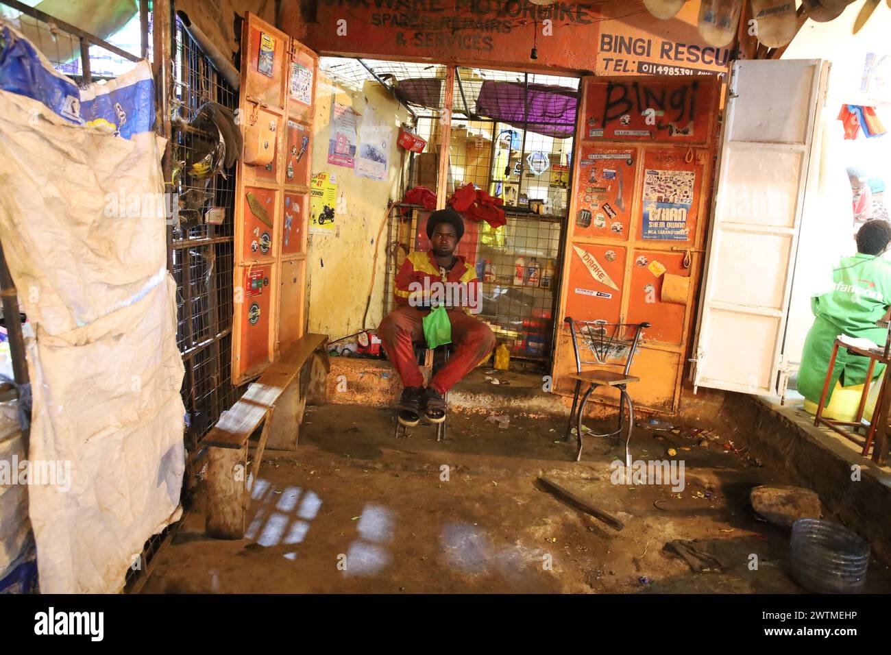 A motorcycle mechanic is seated waiting outside his shop in Kibera Slum ...