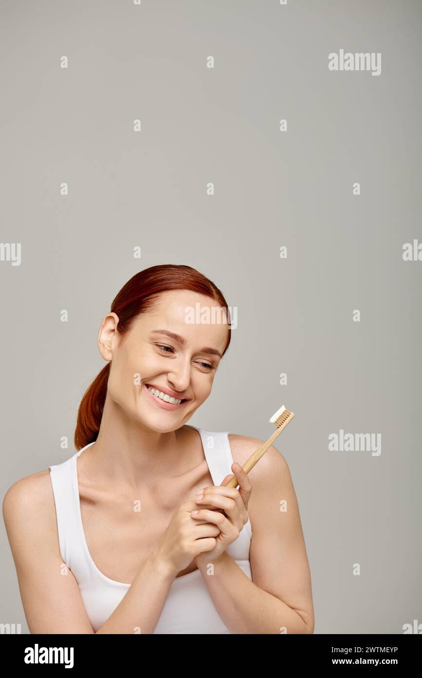 woman with red hair looking at bamboo toothbrush with toothpaste on ...