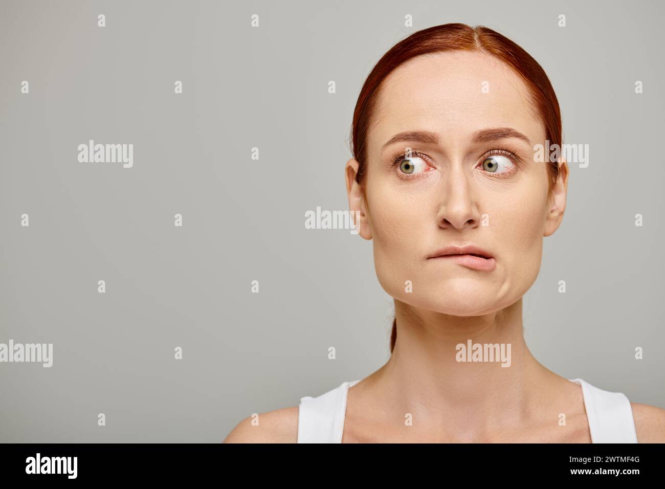 redhead and worried woman in white tank top embodying concern on grey ...