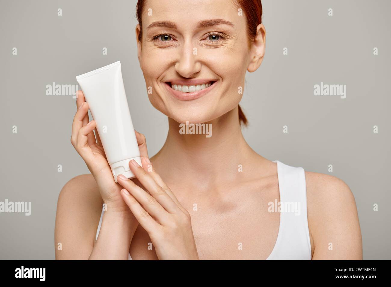 Redhead young and happy woman in 30s holding tube with body lotion on ...