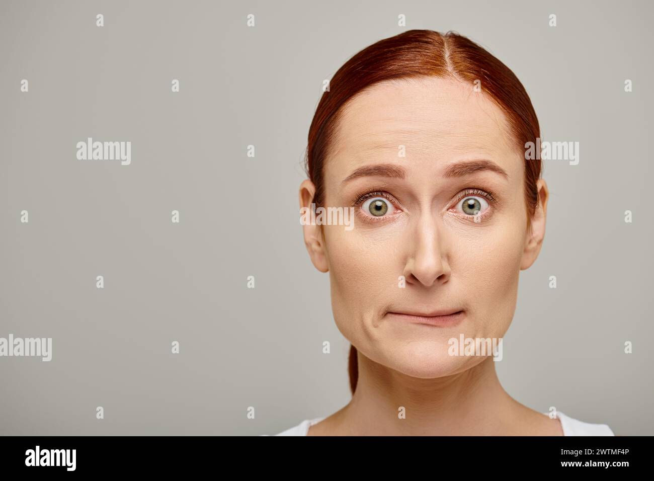 redhead and worried woman in white tank top embodying concern on grey ...