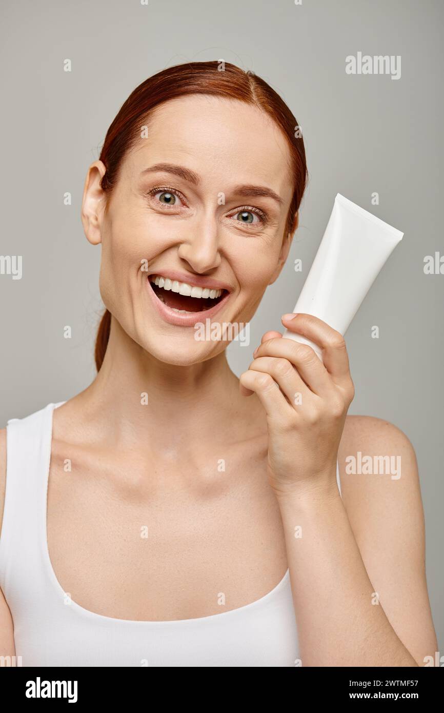 Redhead young and excited woman in 30s holding tube with body lotion on ...