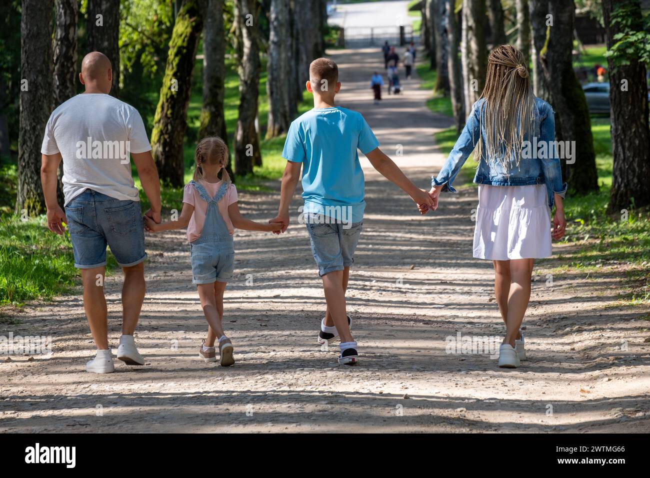 A family stroll down a tree-lined path, joy as parents swing their ...