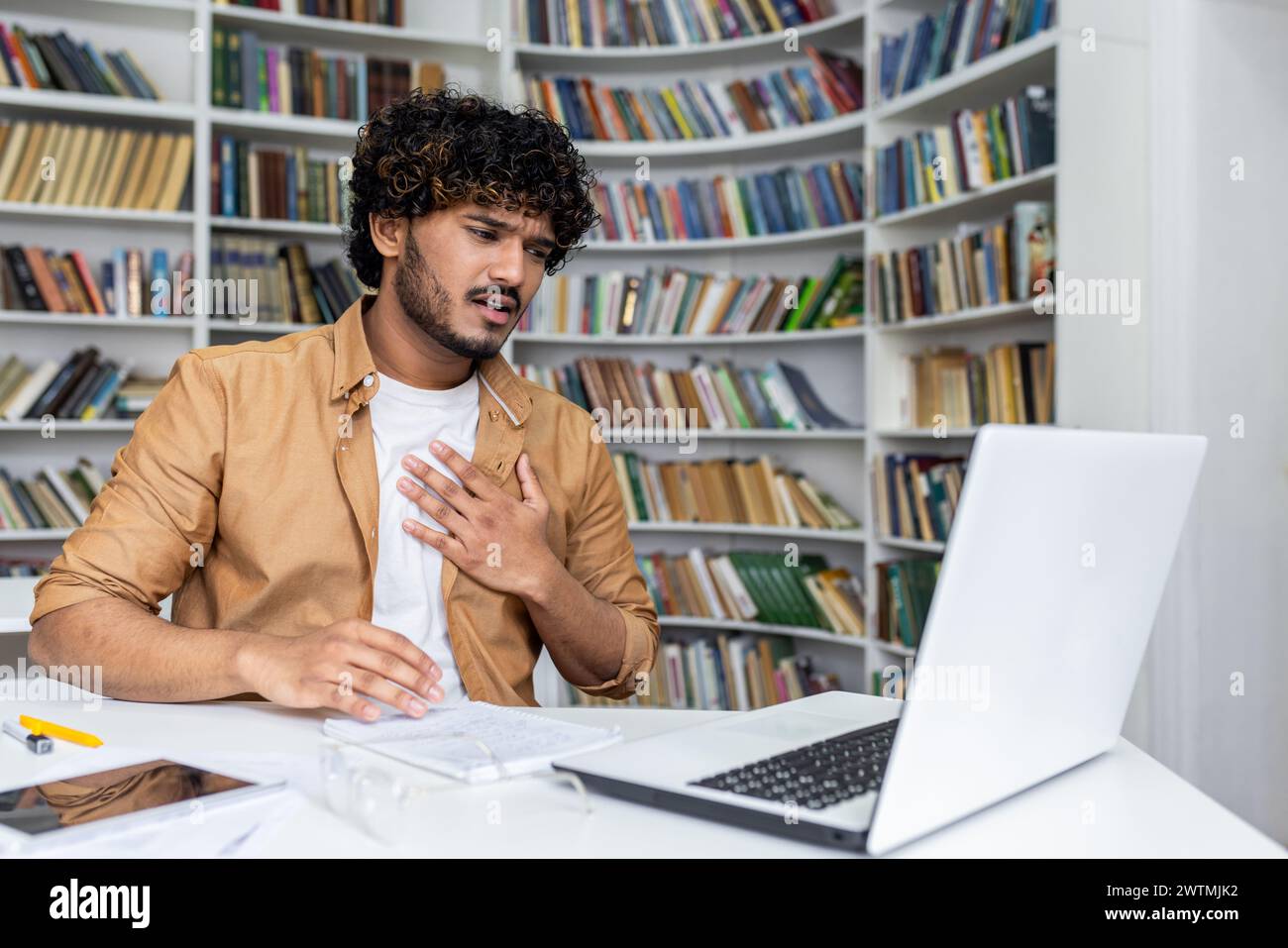 Millennial curly man in shirt sitting by desktop with portable computer ...