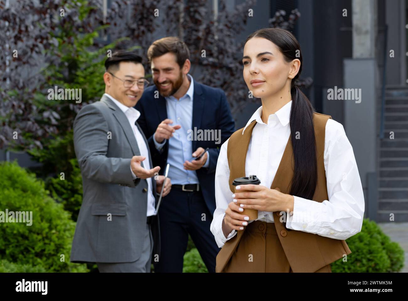 Attractive woman with coffee cup passing by two men in business suits ...