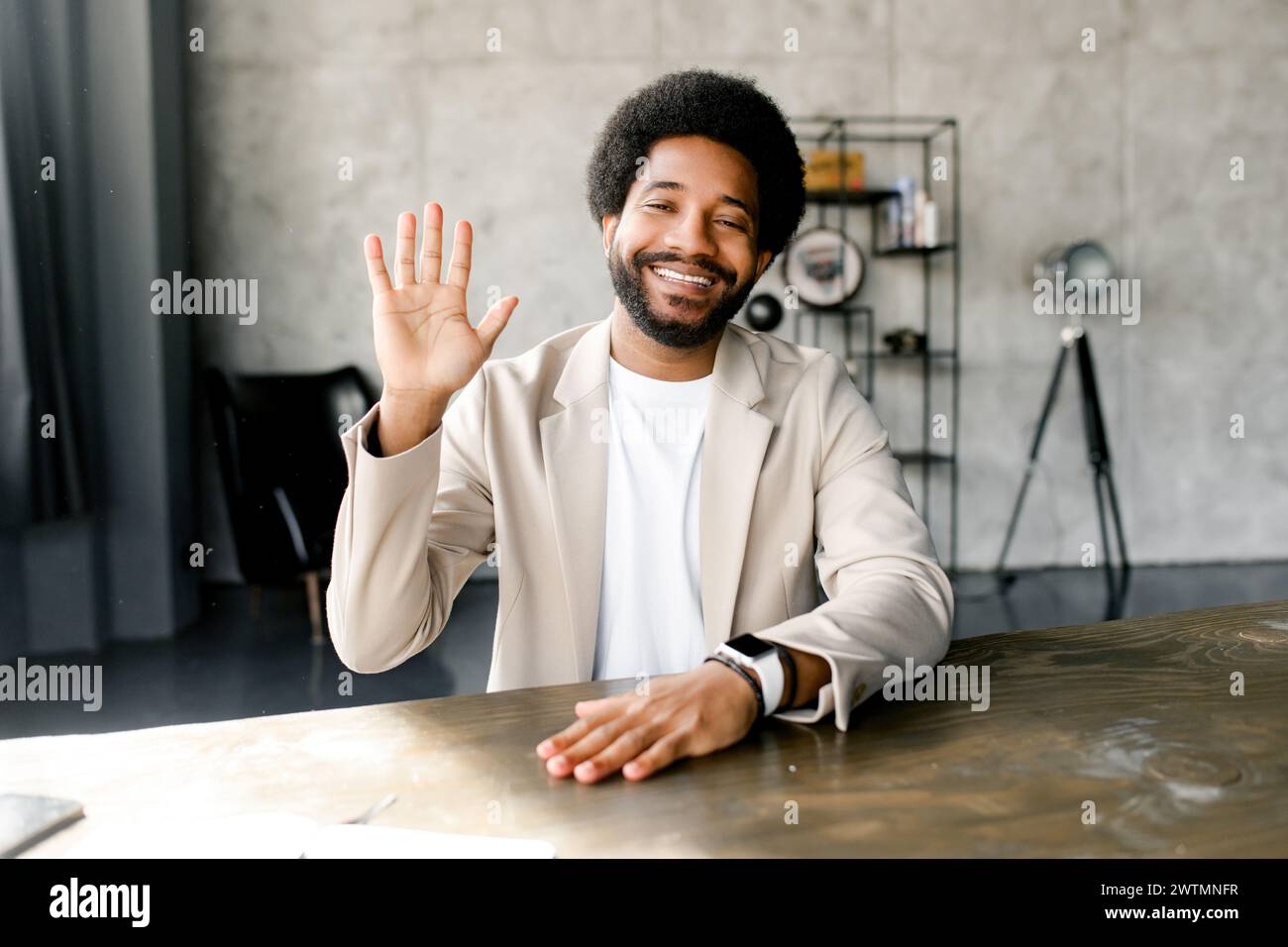 Young businessman waves hello with a warm, inviting smile, positioned ...