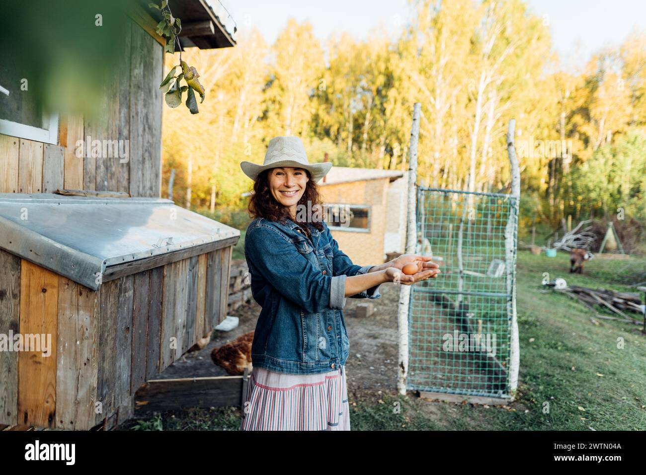 A curly-haired woman in farm clothes beams as she takes an egg from ...