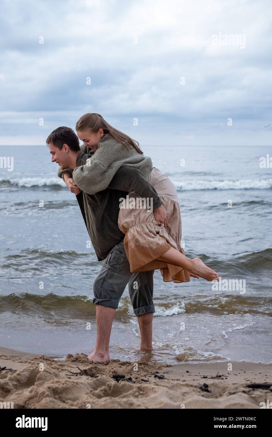 A couple engages in a playful piggyback ride on a sandy beach ...