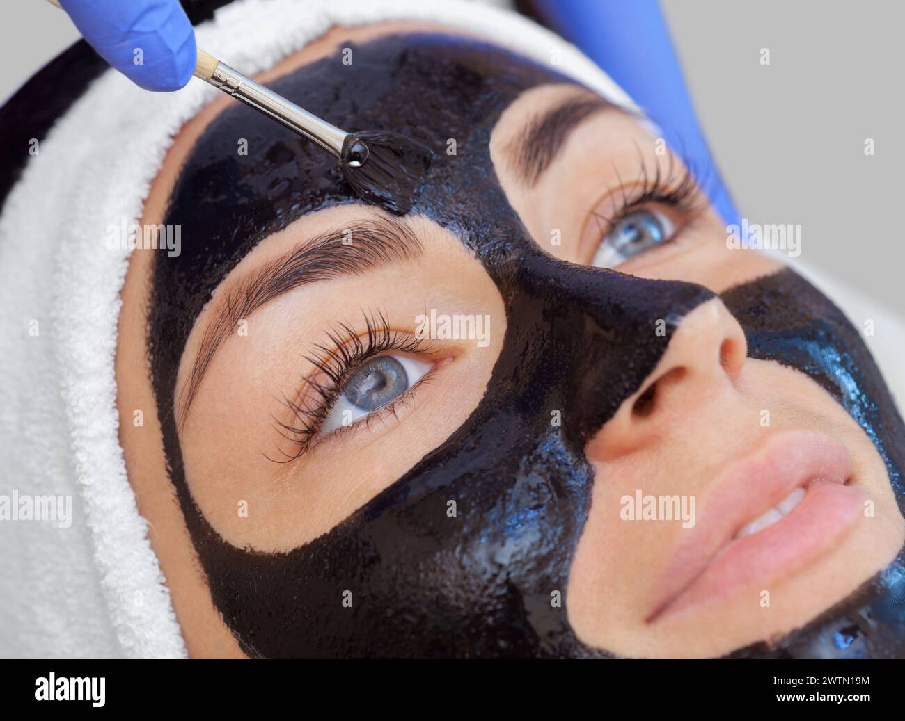 The procedure for applying a black mask to the face of a beautiful ...