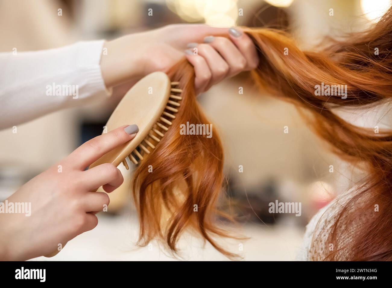 Hairdresser combing her long, red hair of his client in the beauty ...
