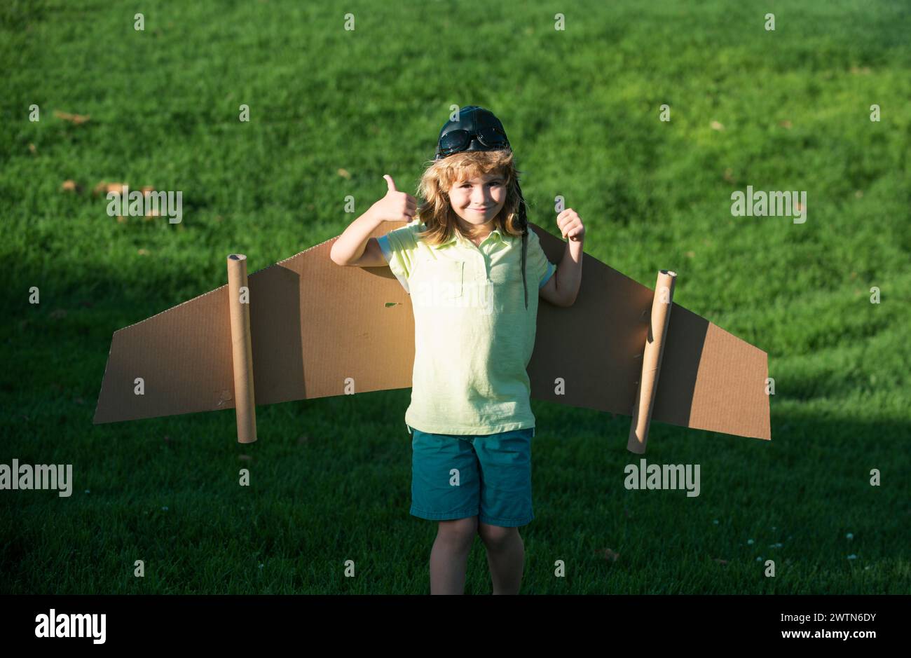 Child boy like a pilot with toy wings against green grass. Kids freedom ...