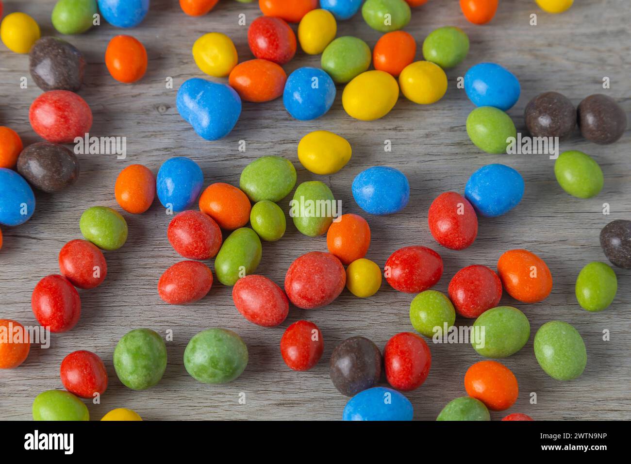Peanuts in chocolate multi-colored glaze on a wooden table. Top view ...