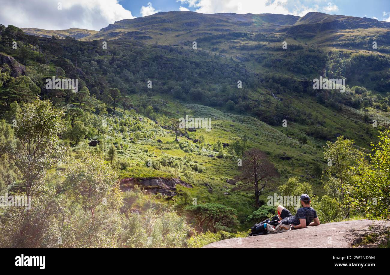 A traveler rests on a rock in the sun in front of the Ben Nevis ...