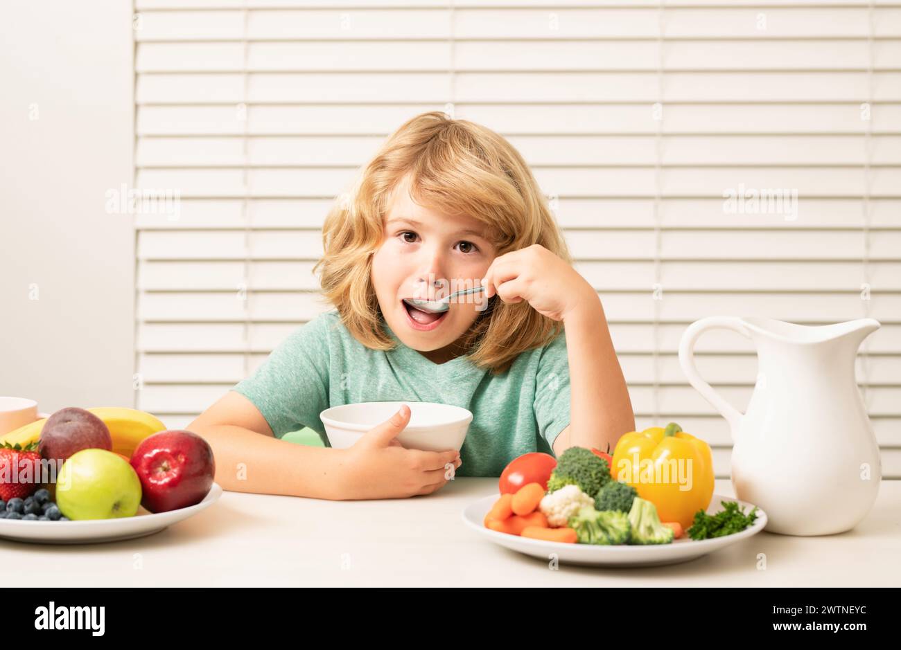 Kid preteen boy in the kitchen at the table eating vegetable and fruits ...
