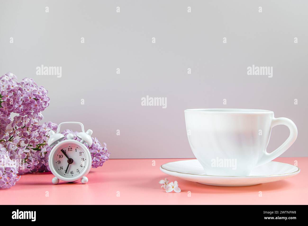 Alarm clock, lilac flowers and cup of coffee on light background ...