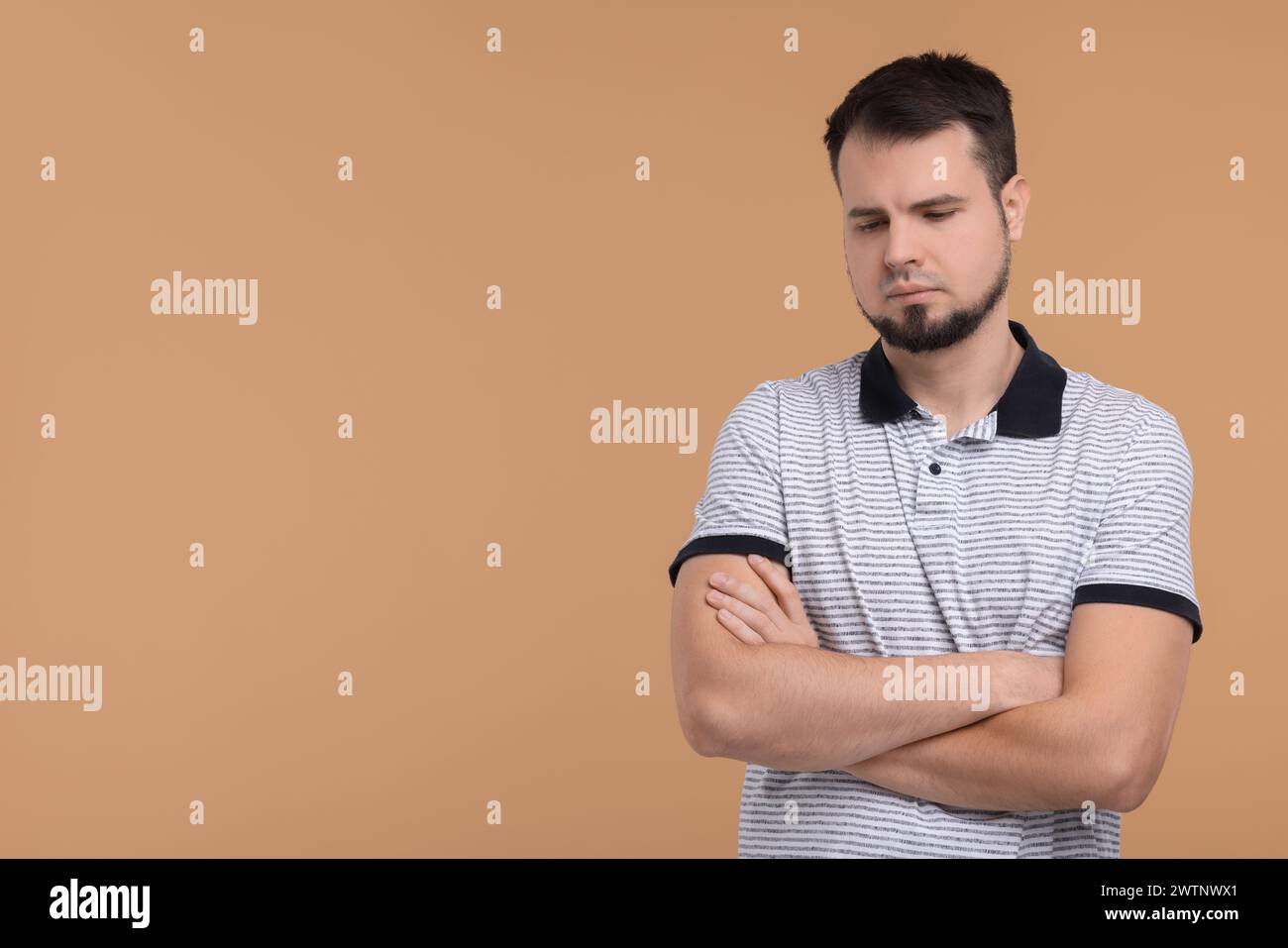 Portrait of sad man with crossed arms on beige background, space for ...