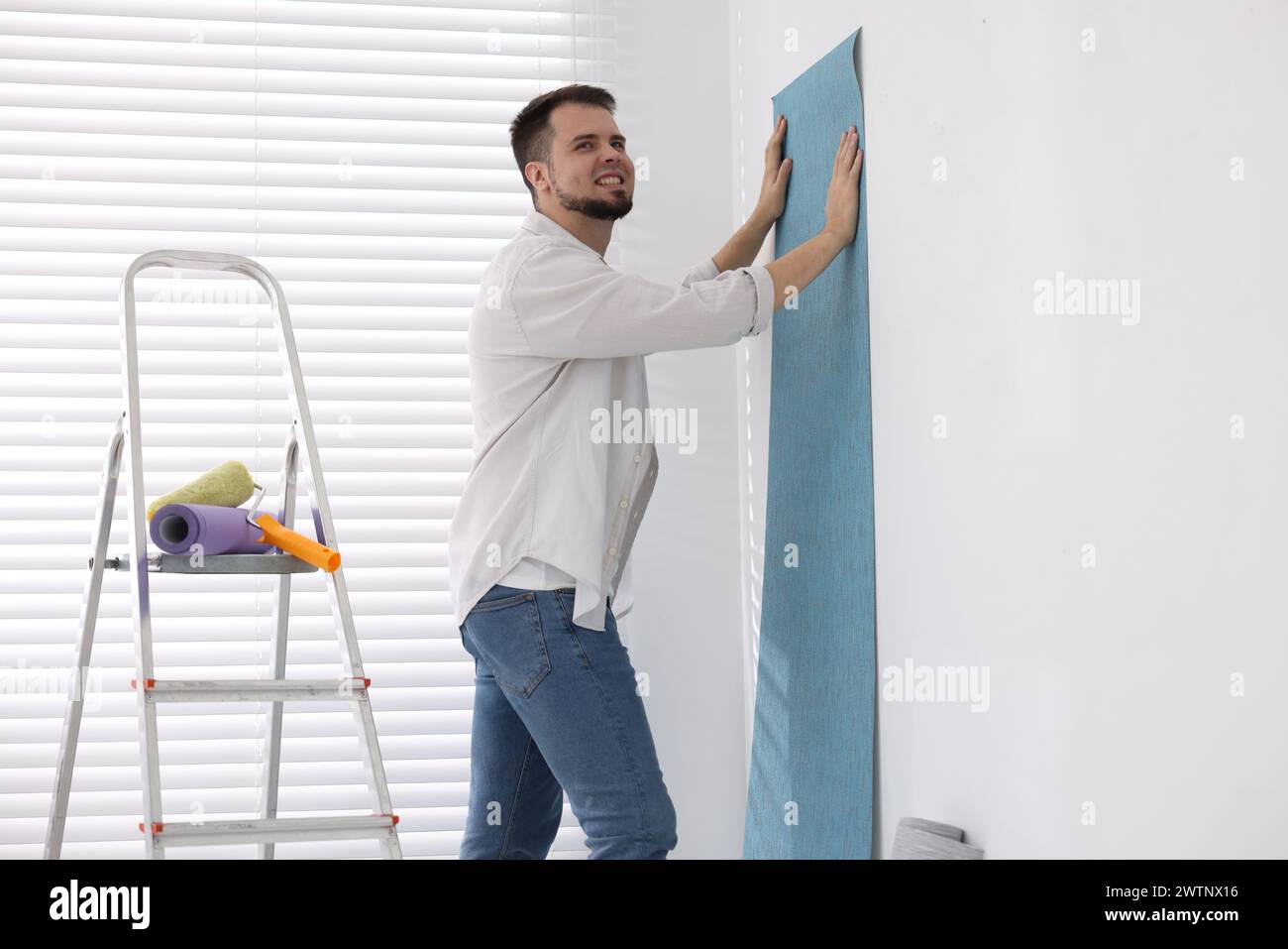 Man hanging light blue wallpaper in room Stock Photo - Alamy