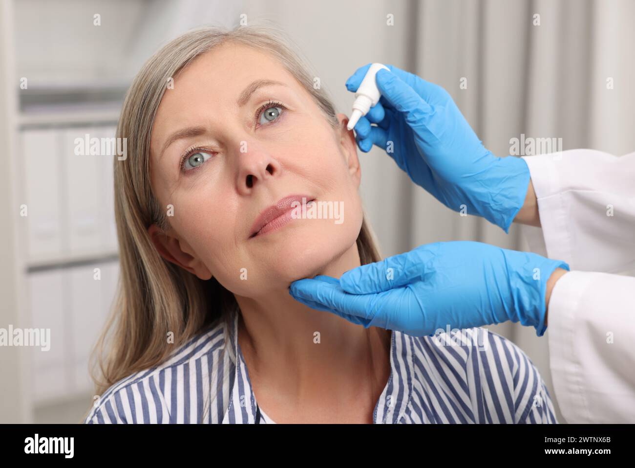 Medical drops. Doctor dripping medication into woman's ear indoors ...