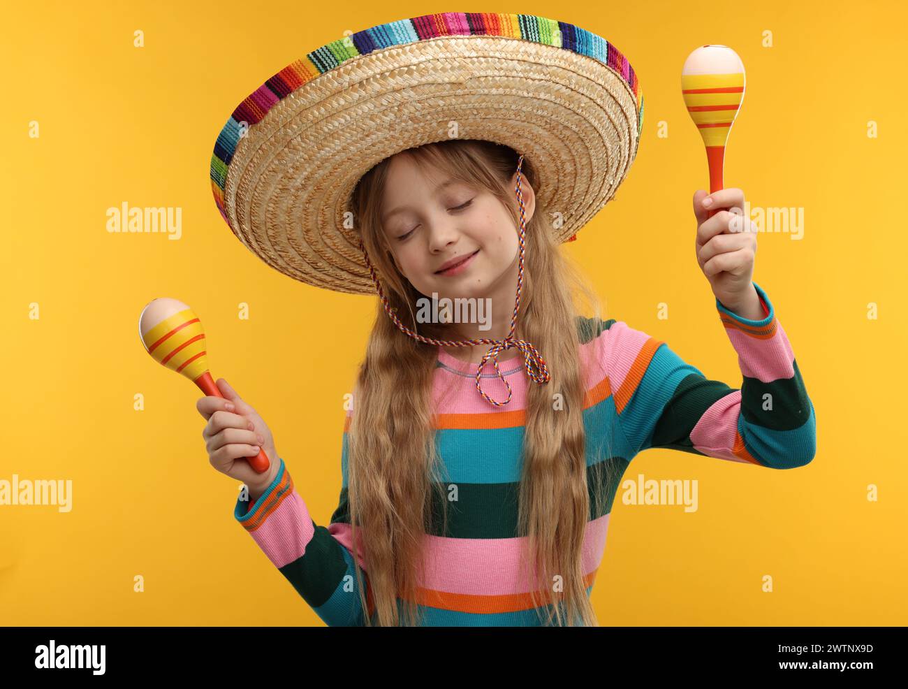 Cute girl in Mexican sombrero hat dancing with maracas on orange ...