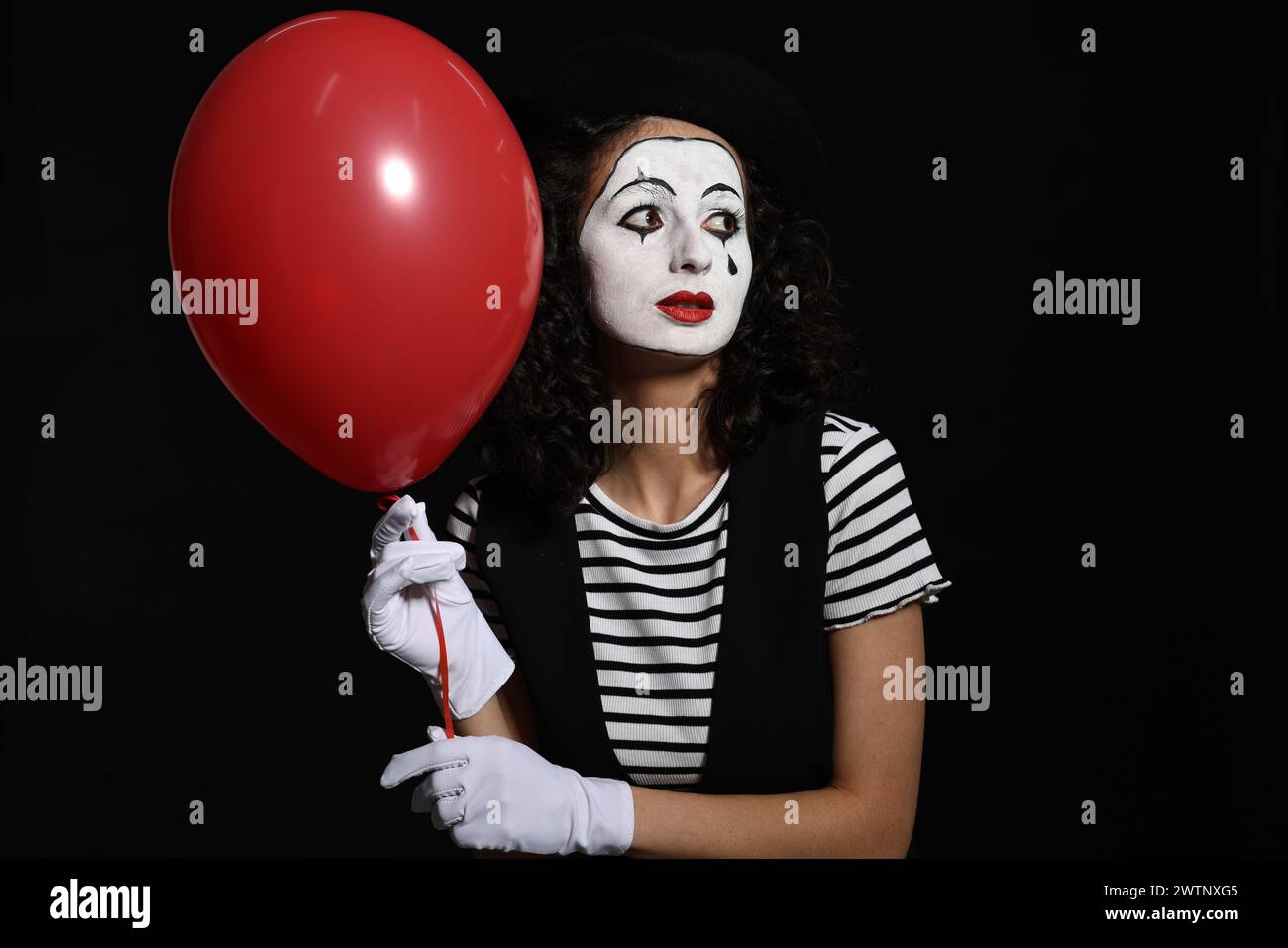 Young woman in mime costume with balloon posing on black background ...