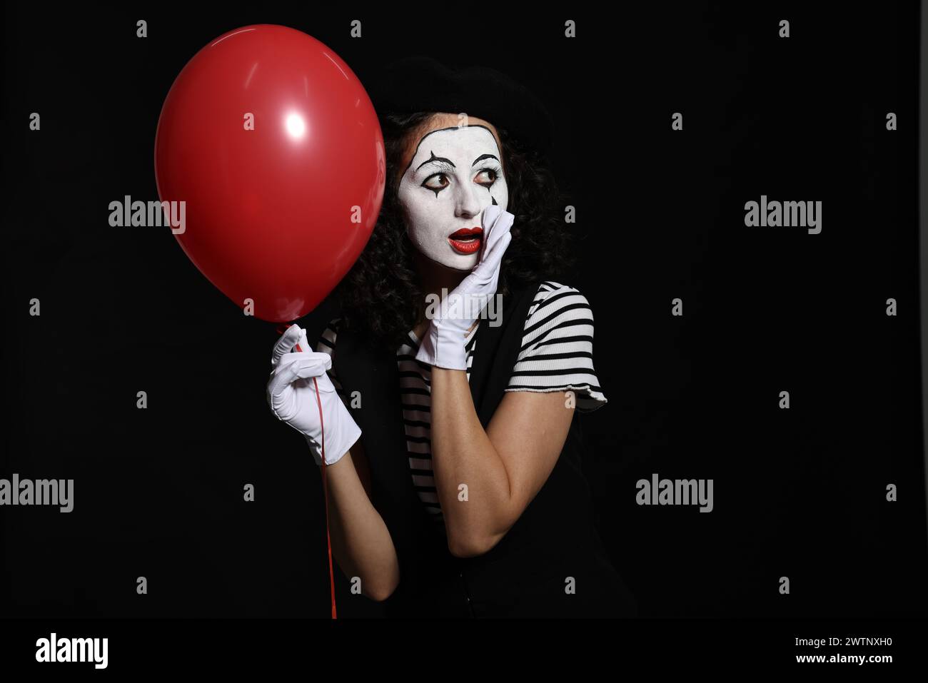 Young woman in mime costume with balloon posing on black background ...