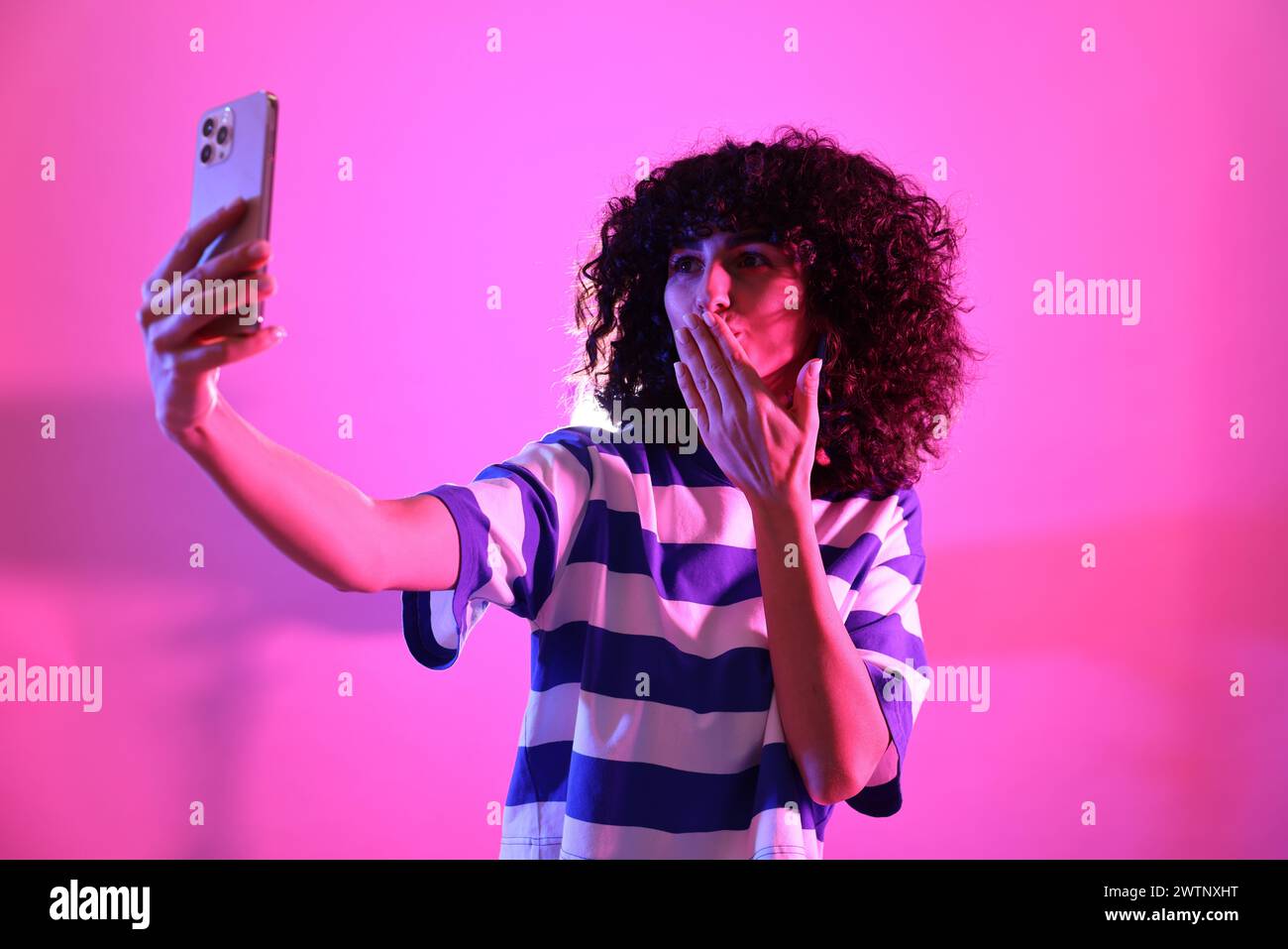 Beautiful young woman taking selfie on color background in neon lights ...