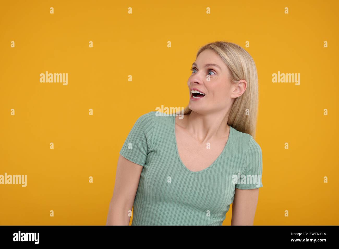 Portrait of happy surprised woman on yellow background, space for text ...
