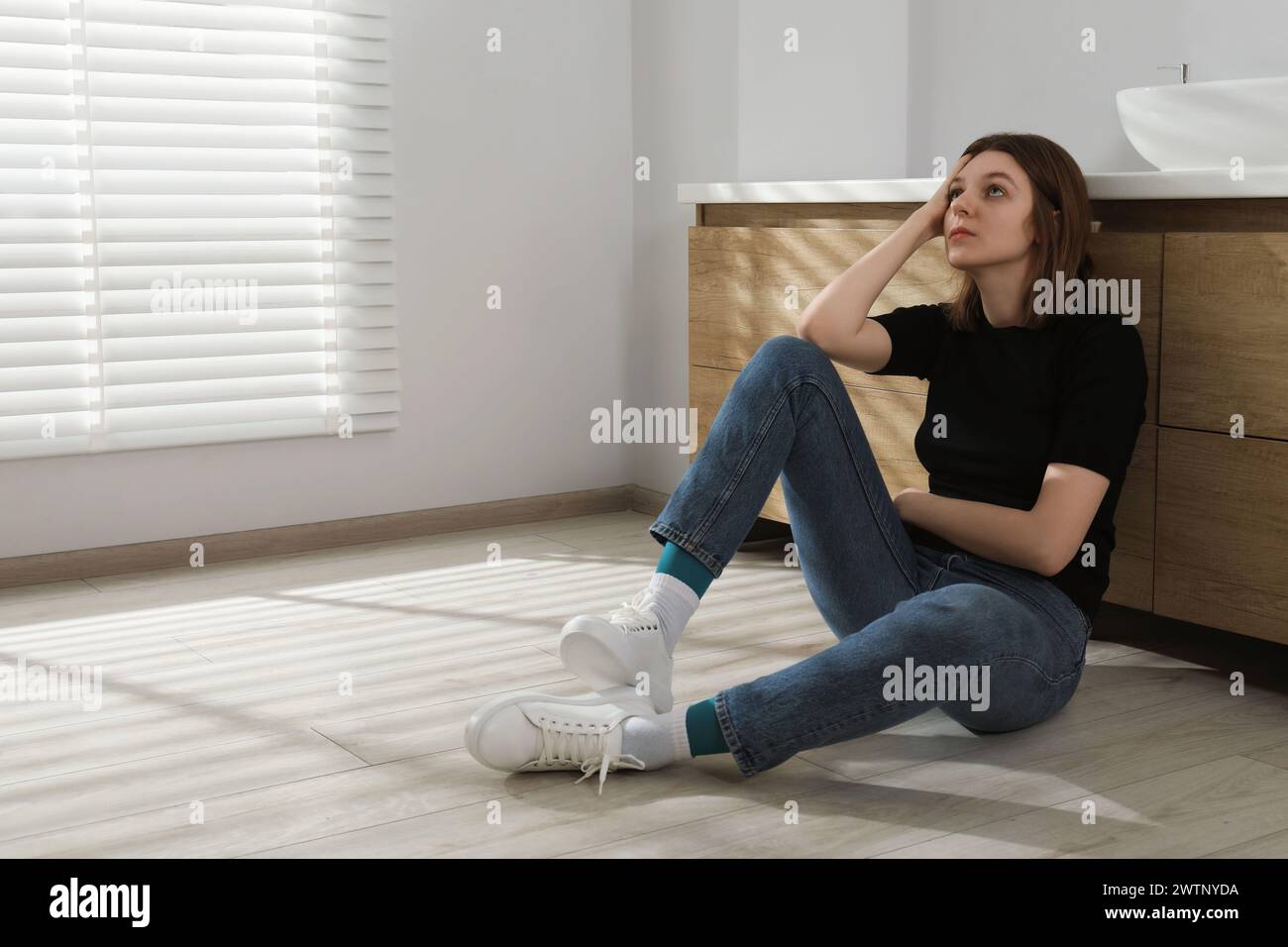 Sad young woman sitting on floor in bathroom, space for text Stock ...