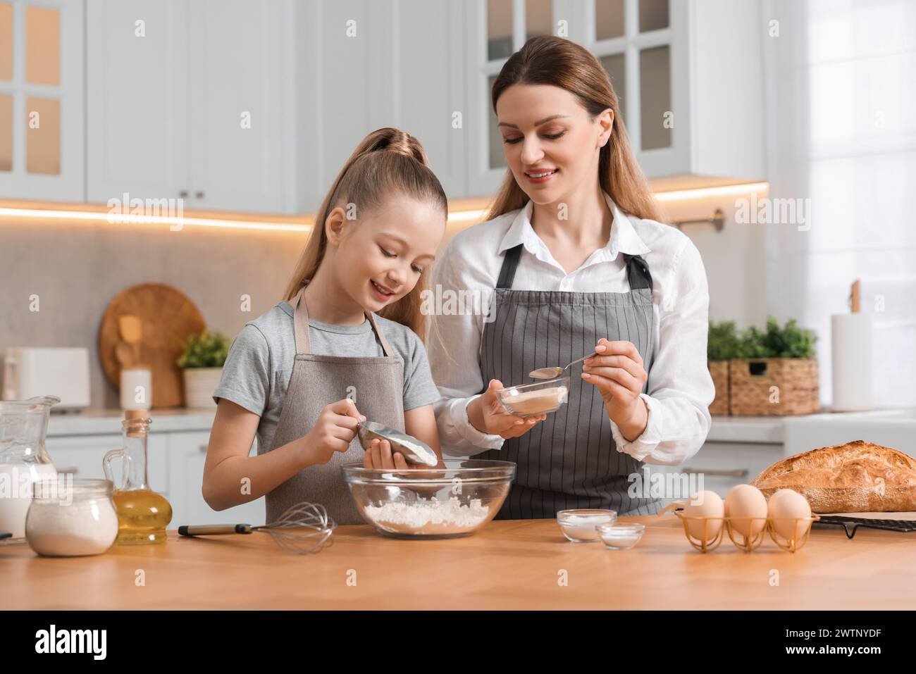 Making bread. Mother and her daughter putting flour and dry yeast into ...