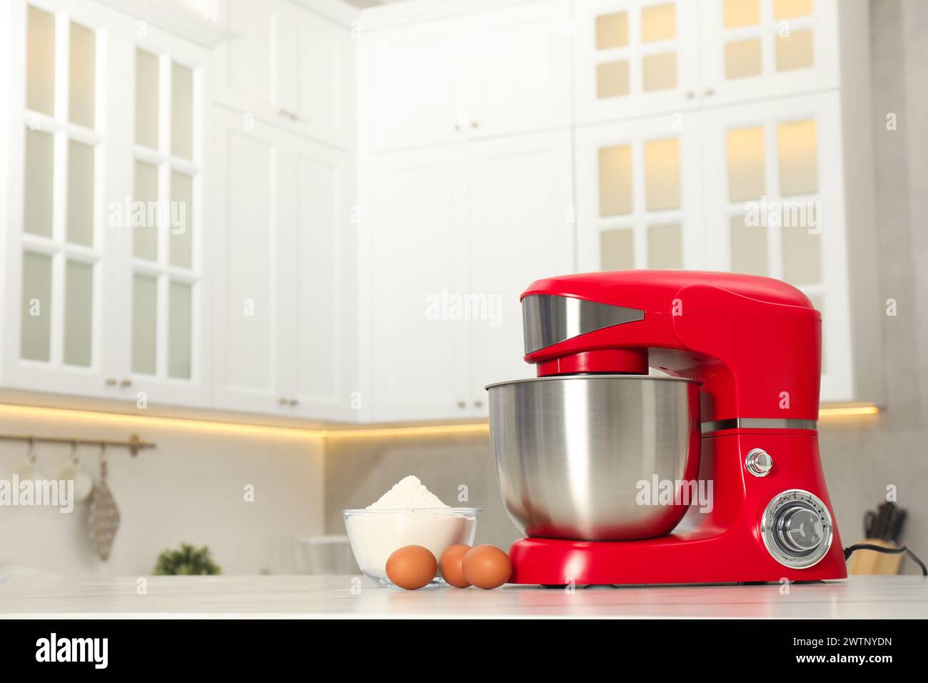 Modern red stand mixer, eggs and bowl with flour on white table in ...
