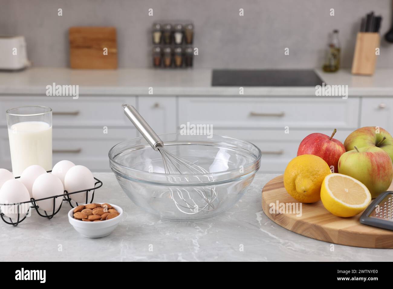 Metal whisk, bowl and different products on gray marble table in ...
