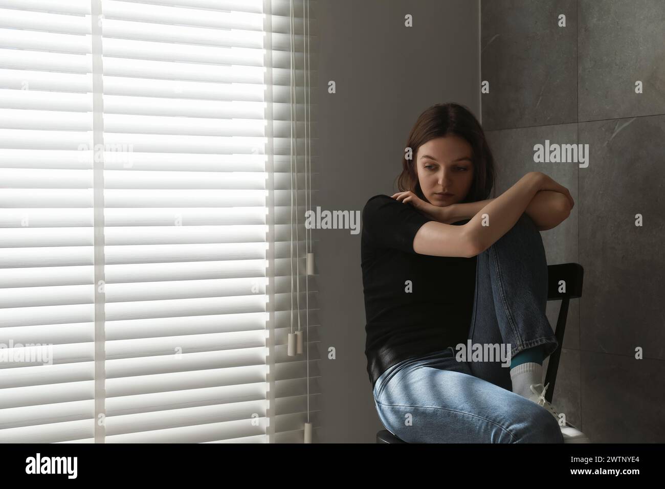 Sad young woman sitting on chair indoors, space for text Stock Photo ...