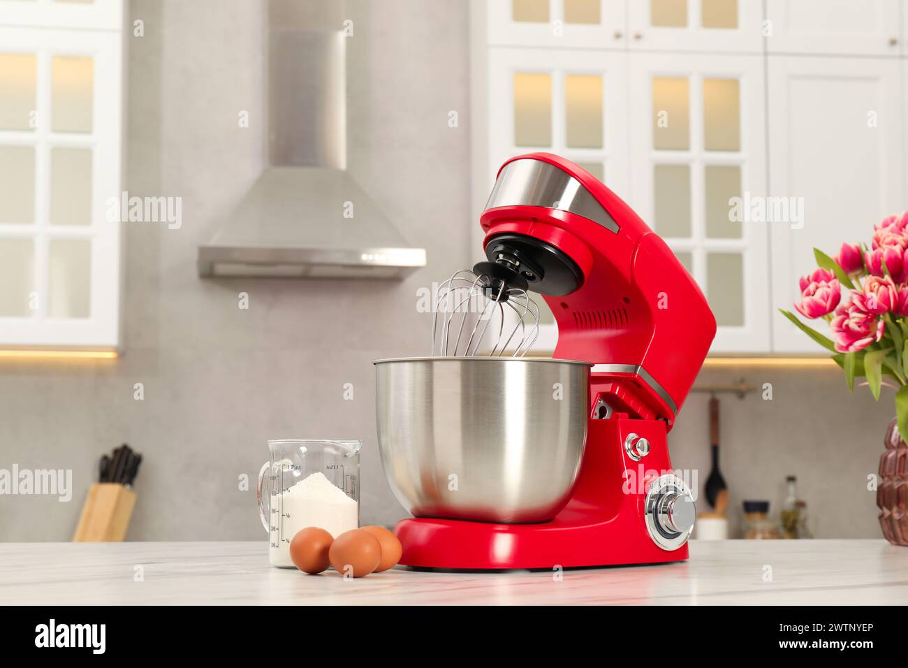 Modern red stand mixer, eggs and container with flour on white marble ...