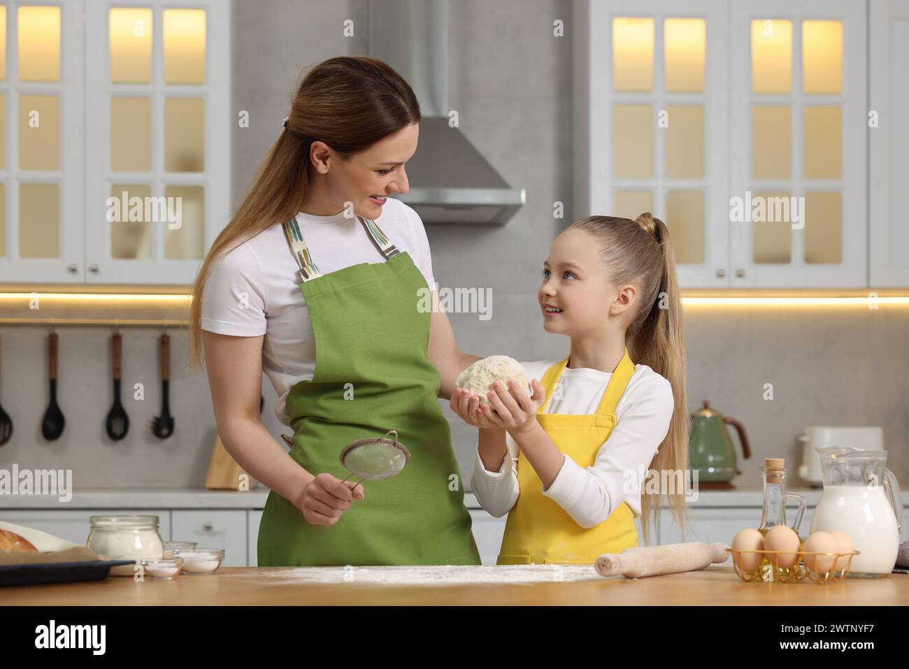 Making bread. Mother and her daughter kneading dough at wooden table in ...