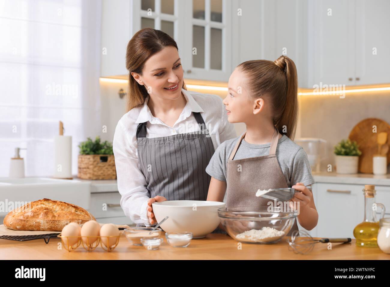 Making bread. Mother and her daughter preparing dough at wooden table ...