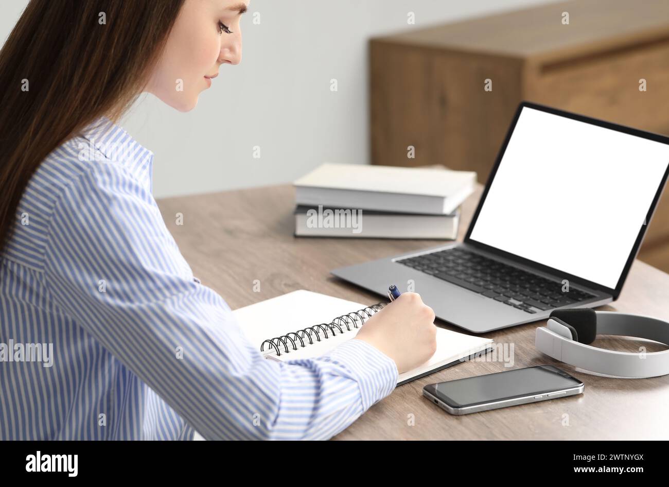 E-learning. woman taking notes during online lesson at table indoors ...