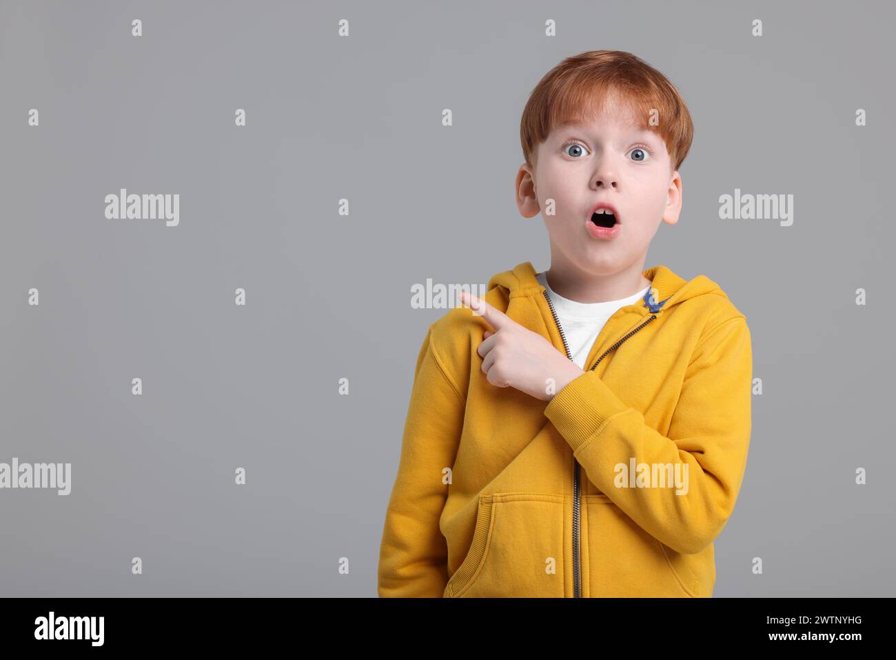 Surprised little boy pointing at something on grey background, space ...