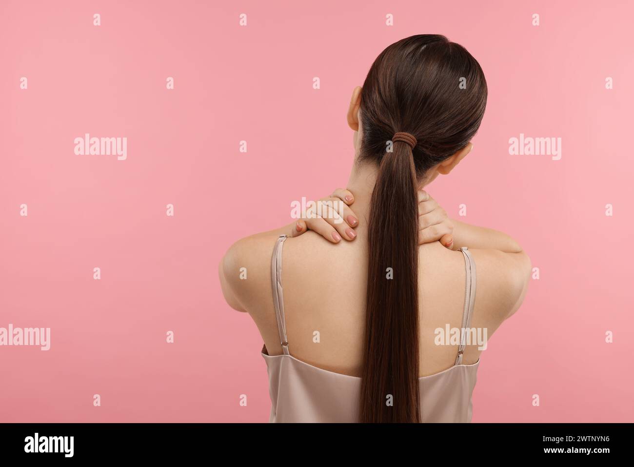 Woman touching her neck on pink background, back view. Space for text ...