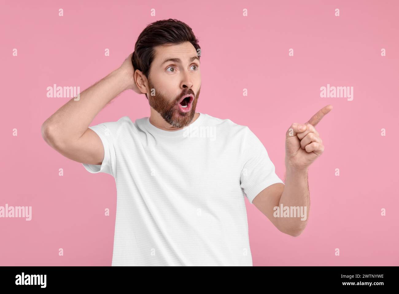 Surprised man pointing at something on pink background Stock Photo - Alamy