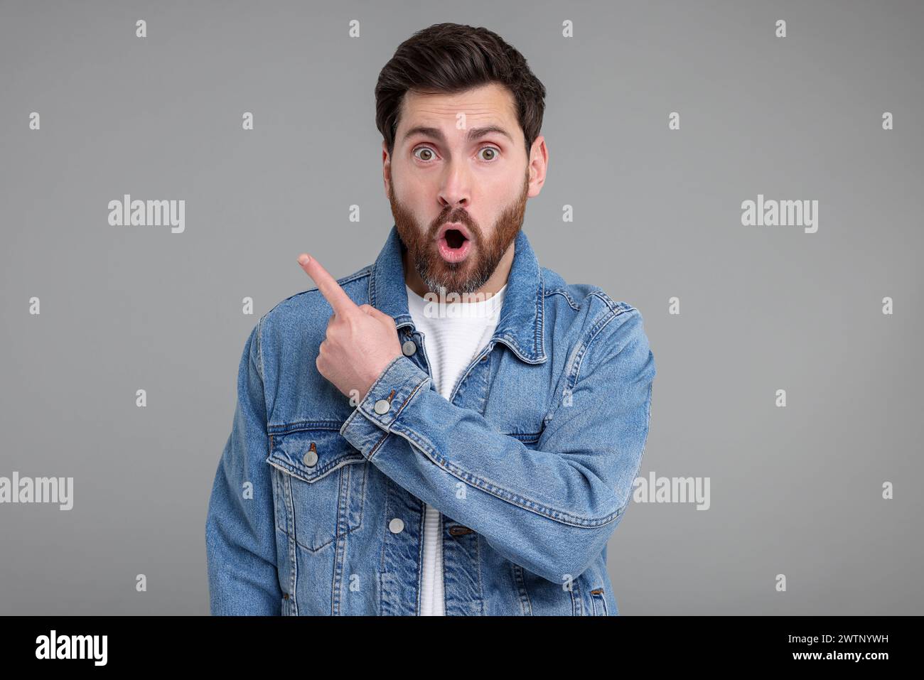 Surprised man pointing at something on grey background Stock Photo - Alamy