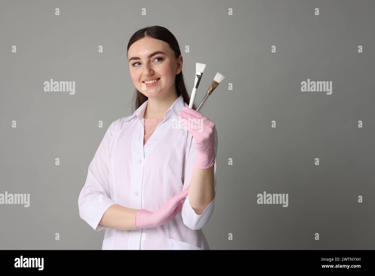 Cosmetologist with cosmetic brushes on grey background, space for text ...