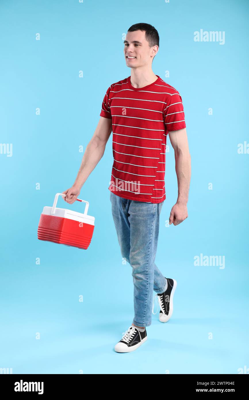 Man with cool box walking on light blue background Stock Photo - Alamy