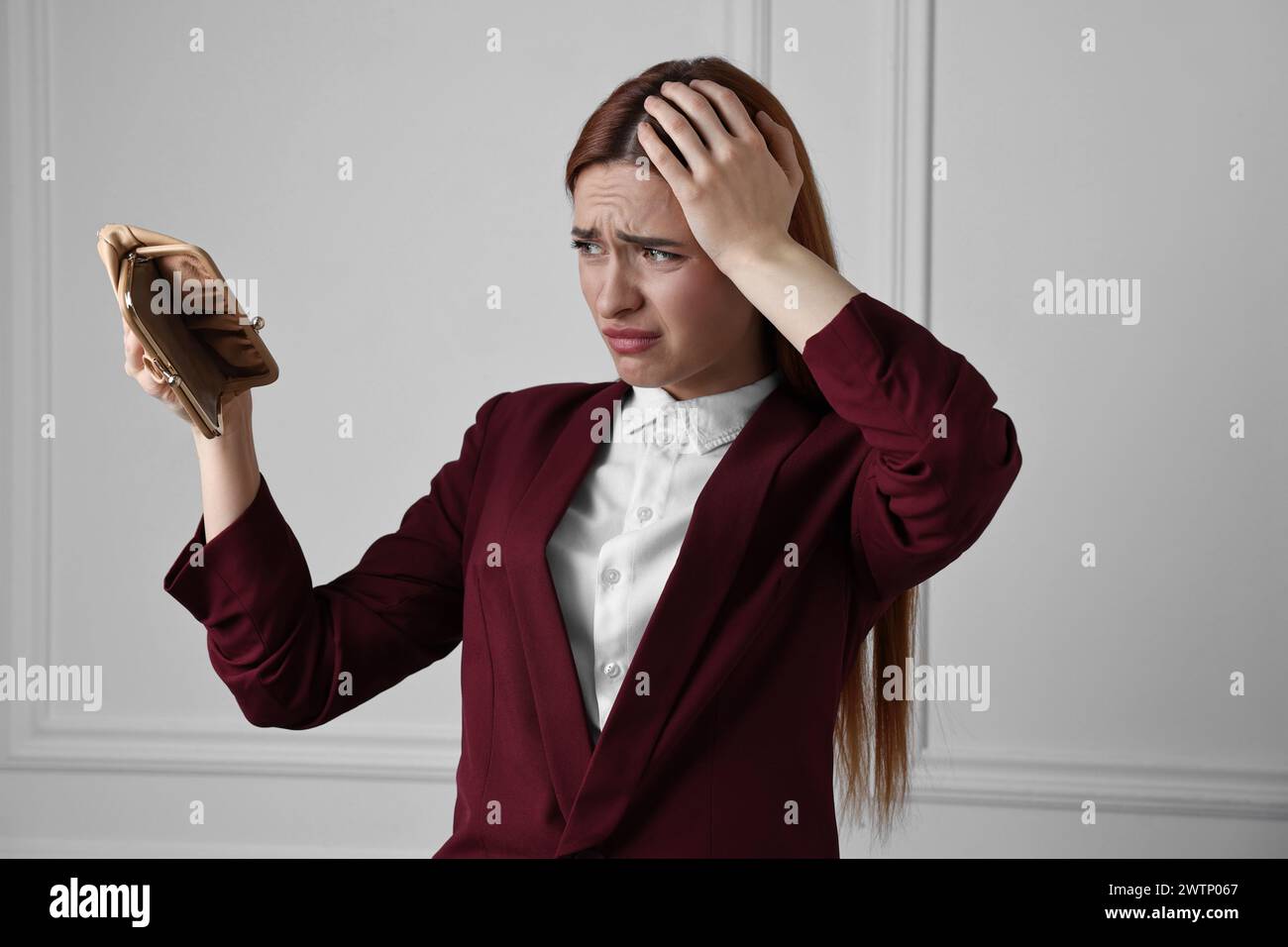 Upset woman with empty wallet near white wall Stock Photo - Alamy