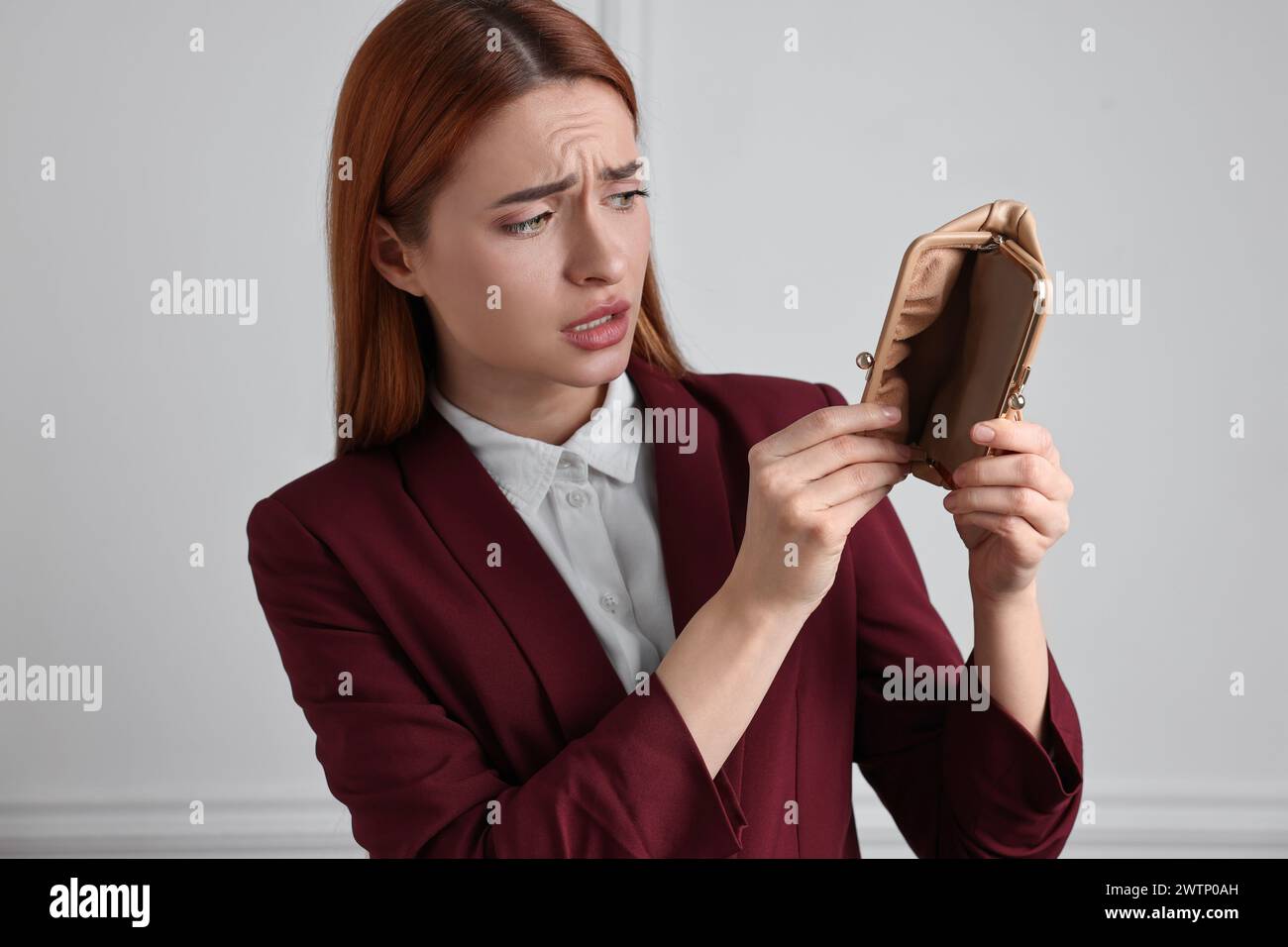 Upset woman with empty wallet near white wall Stock Photo - Alamy