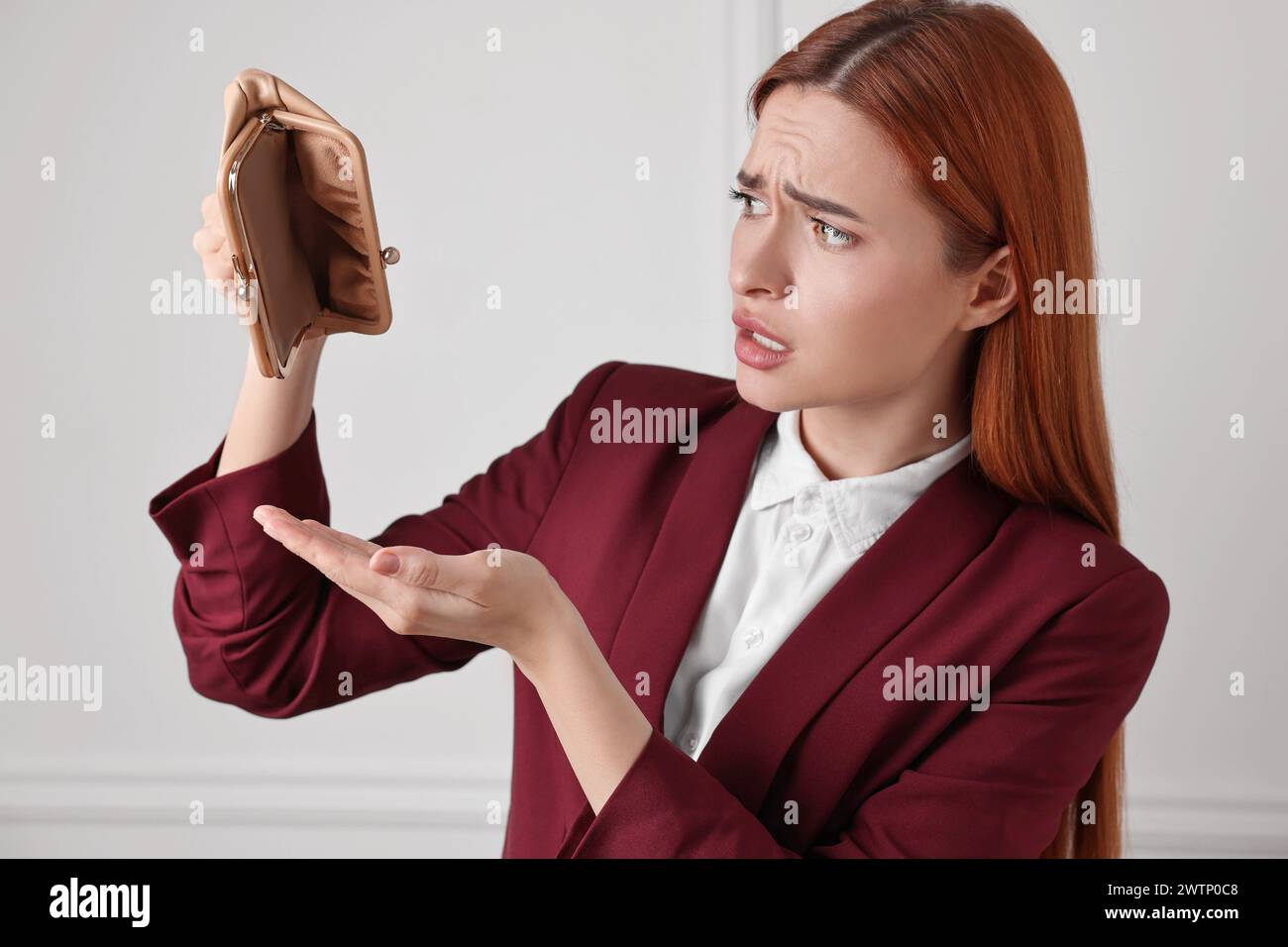 Upset woman with empty wallet near white wall Stock Photo - Alamy