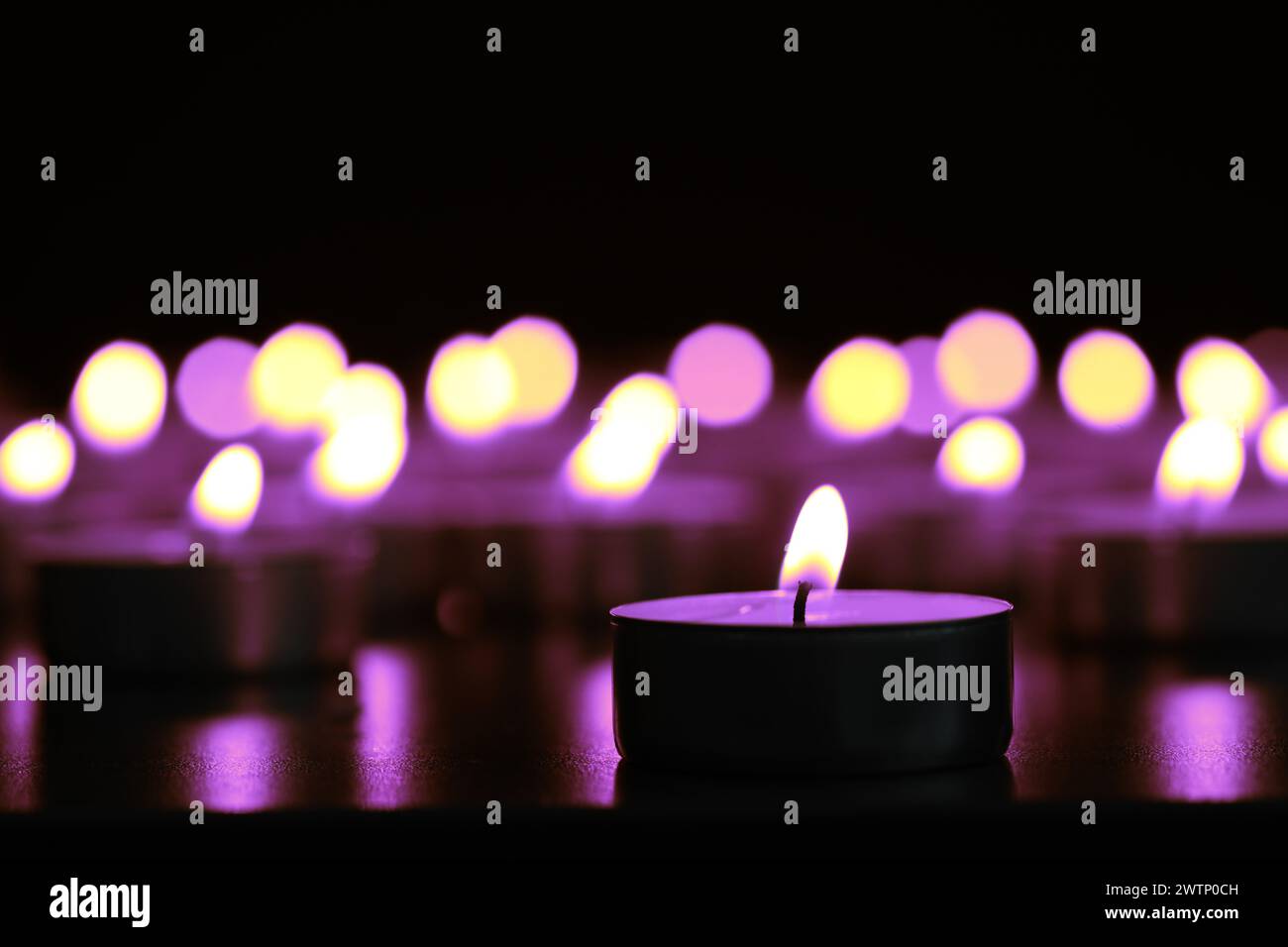 Burning violet candle on black background, closeup. Funeral attributes ...